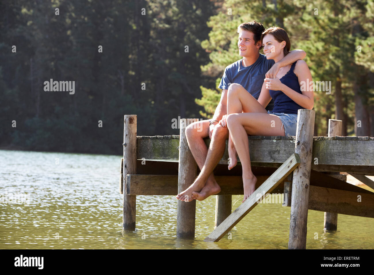 Young Romantic Couple Sitting On Wooden Jetty Looking Out Over Lake ...