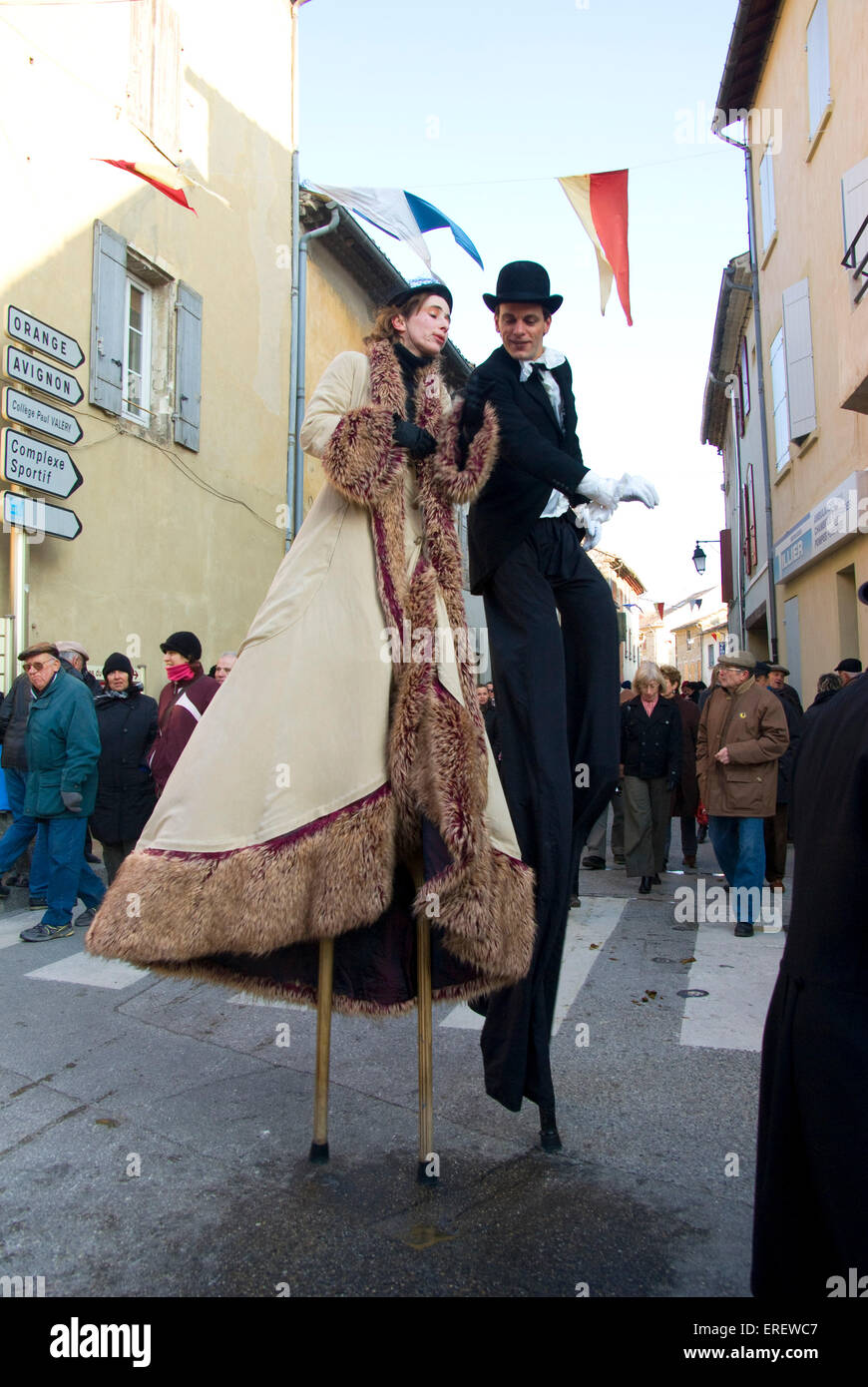 A couple on stilts, woman in long coat and man in tails and top hat ...
