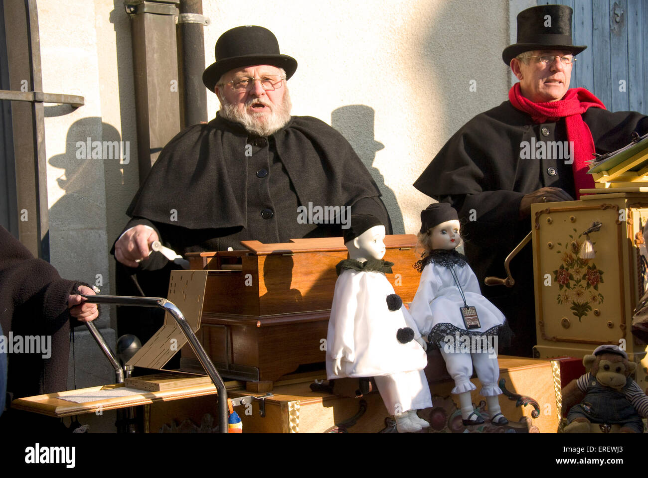 Bearded older man in black cape and bowler hat turning the handle of a ...