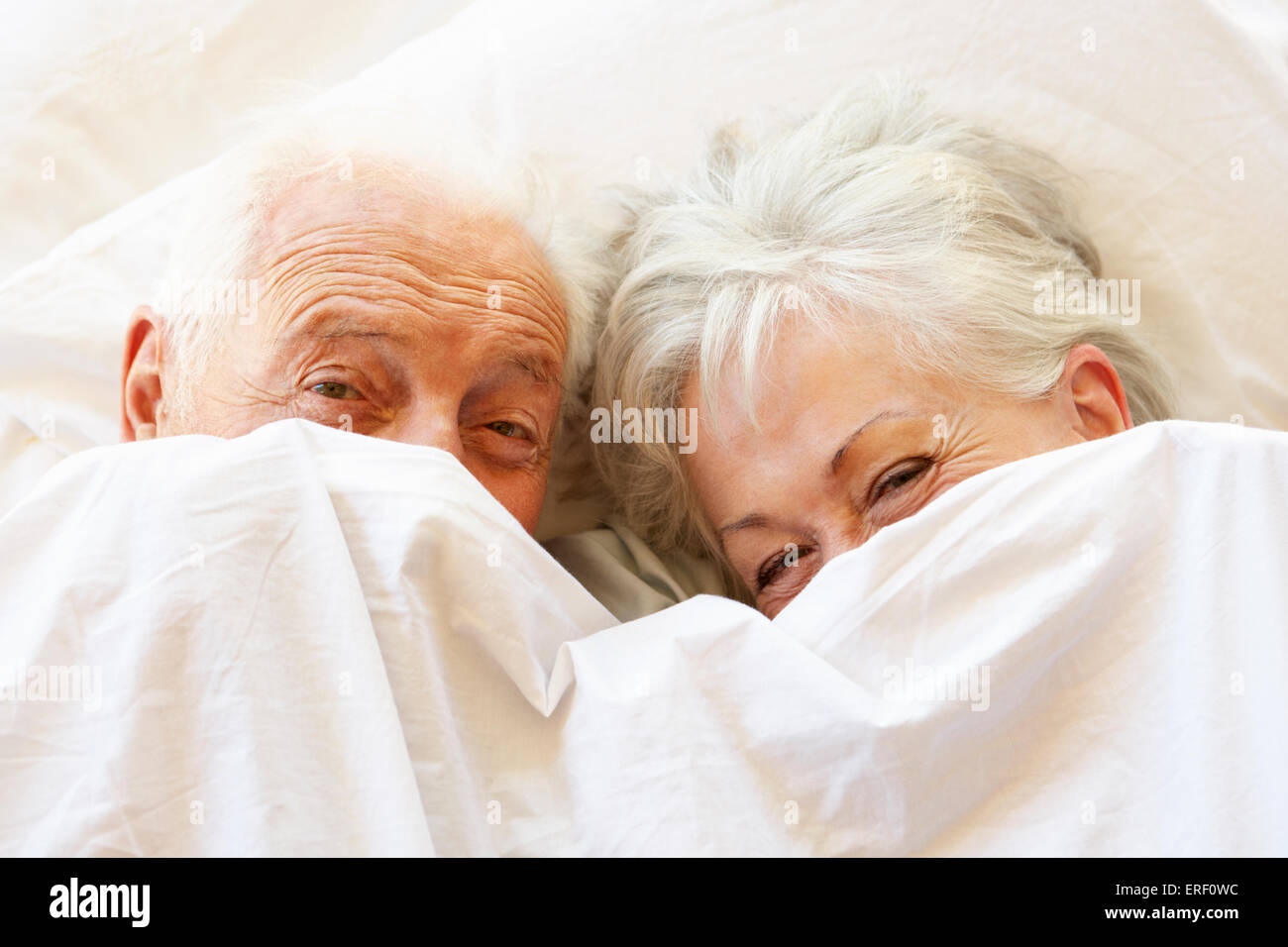 Senior Couple Relaxing In Bed Hiding Under Sheets Stock Photo - Alamy