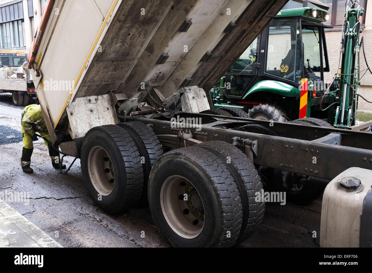 Workman digging out tarmac from the back of a lorry / tipper truck ...
