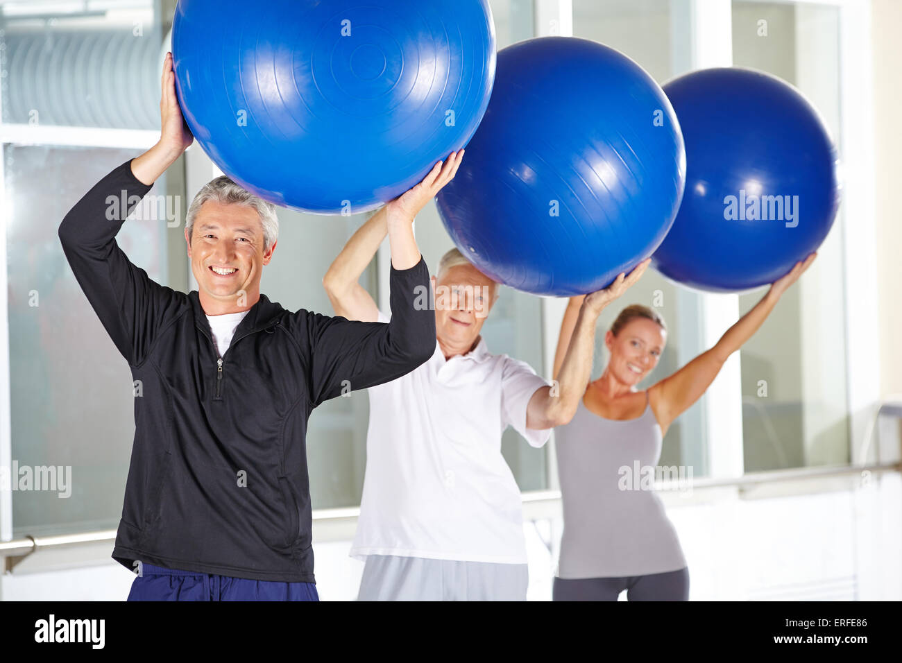 Smiling elderly man exercising with gym ball in fitness center during ...