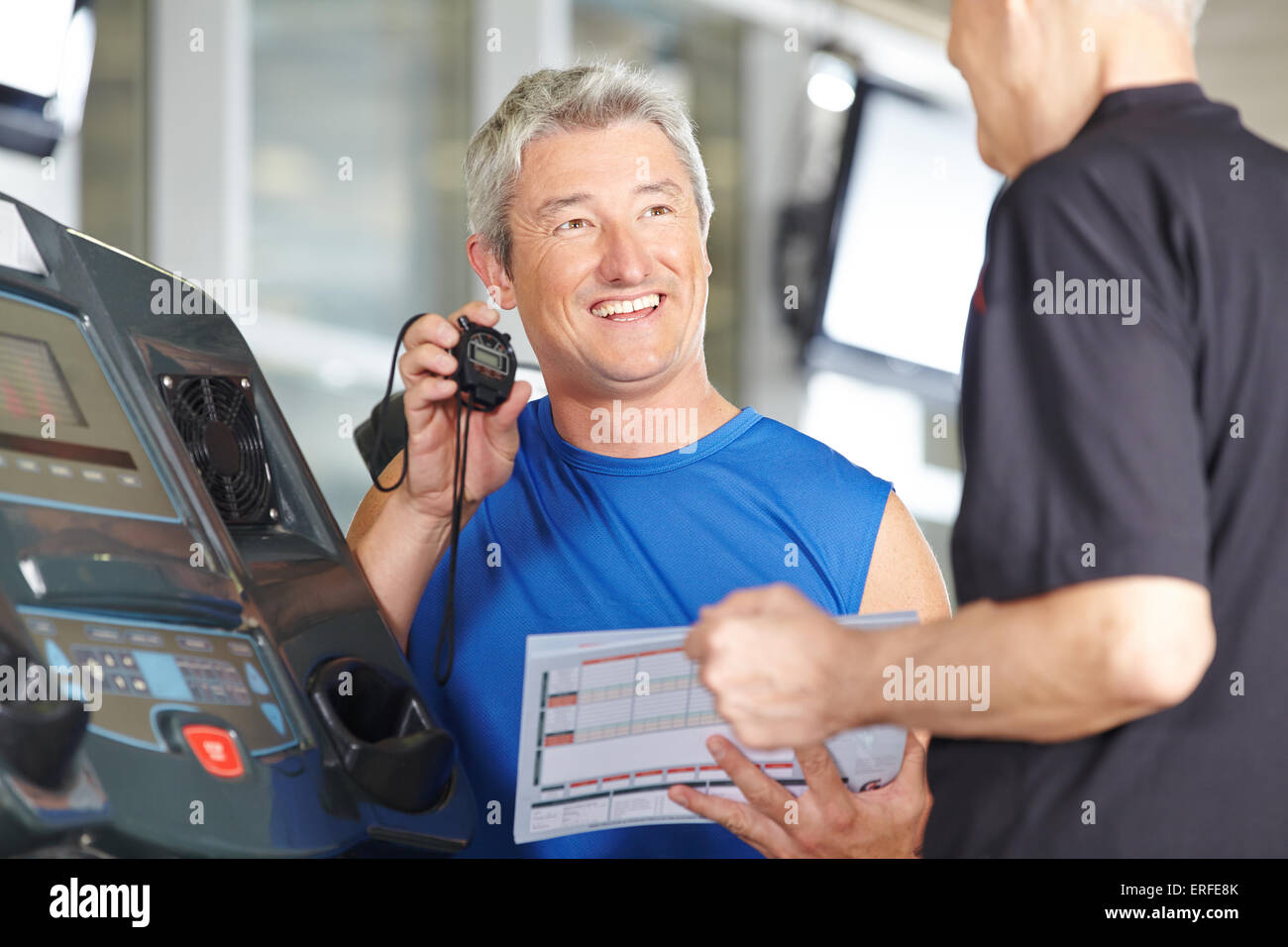 Fitness trainer with stopwatch at treadmill with senior man Stock Photo ...