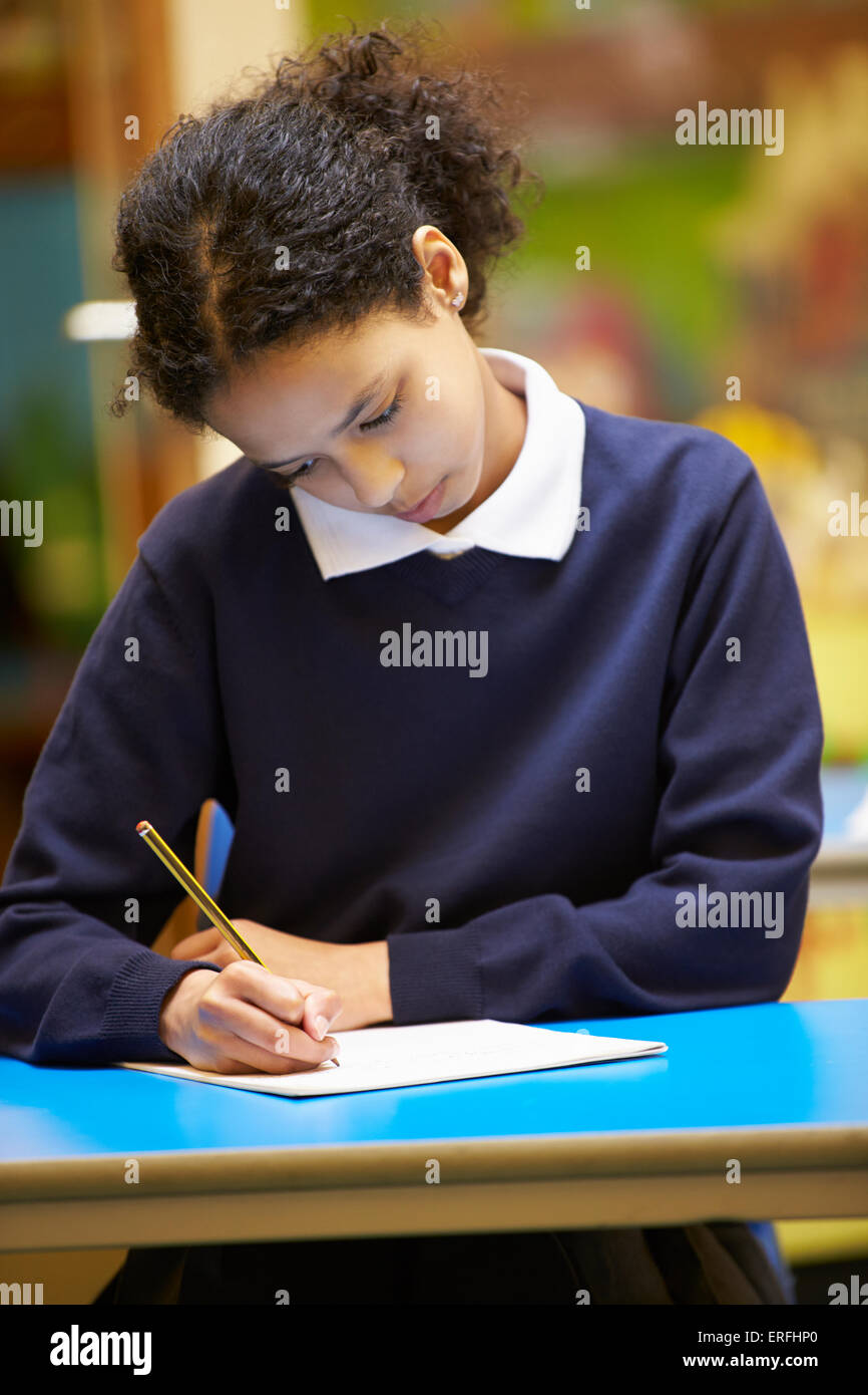 Female Elementary School Pupil Writing Book In Classroom Stock Photo ...