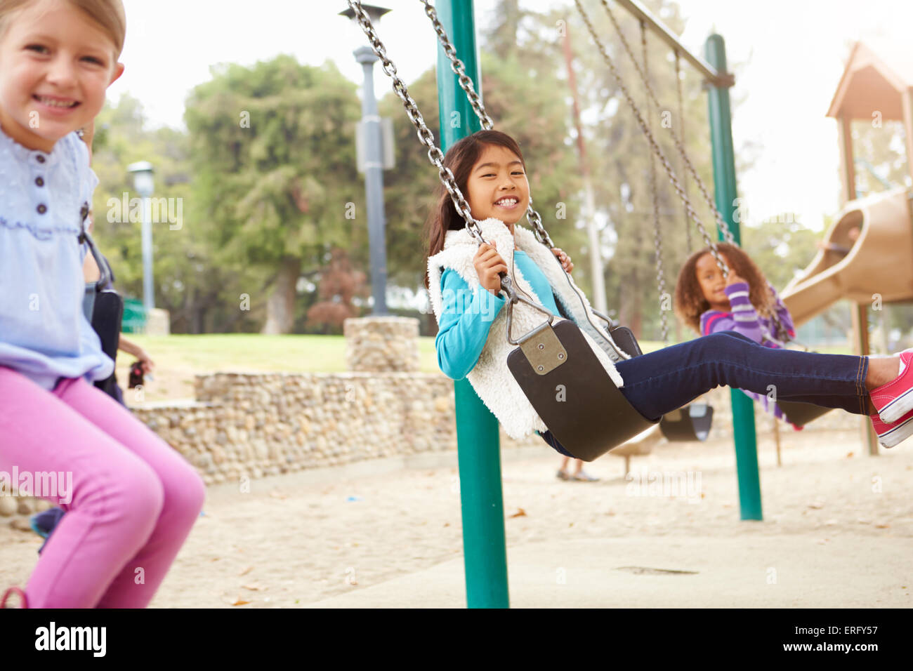 Three Young Girls Playing On Swing In Playground Stock Photo - Alamy