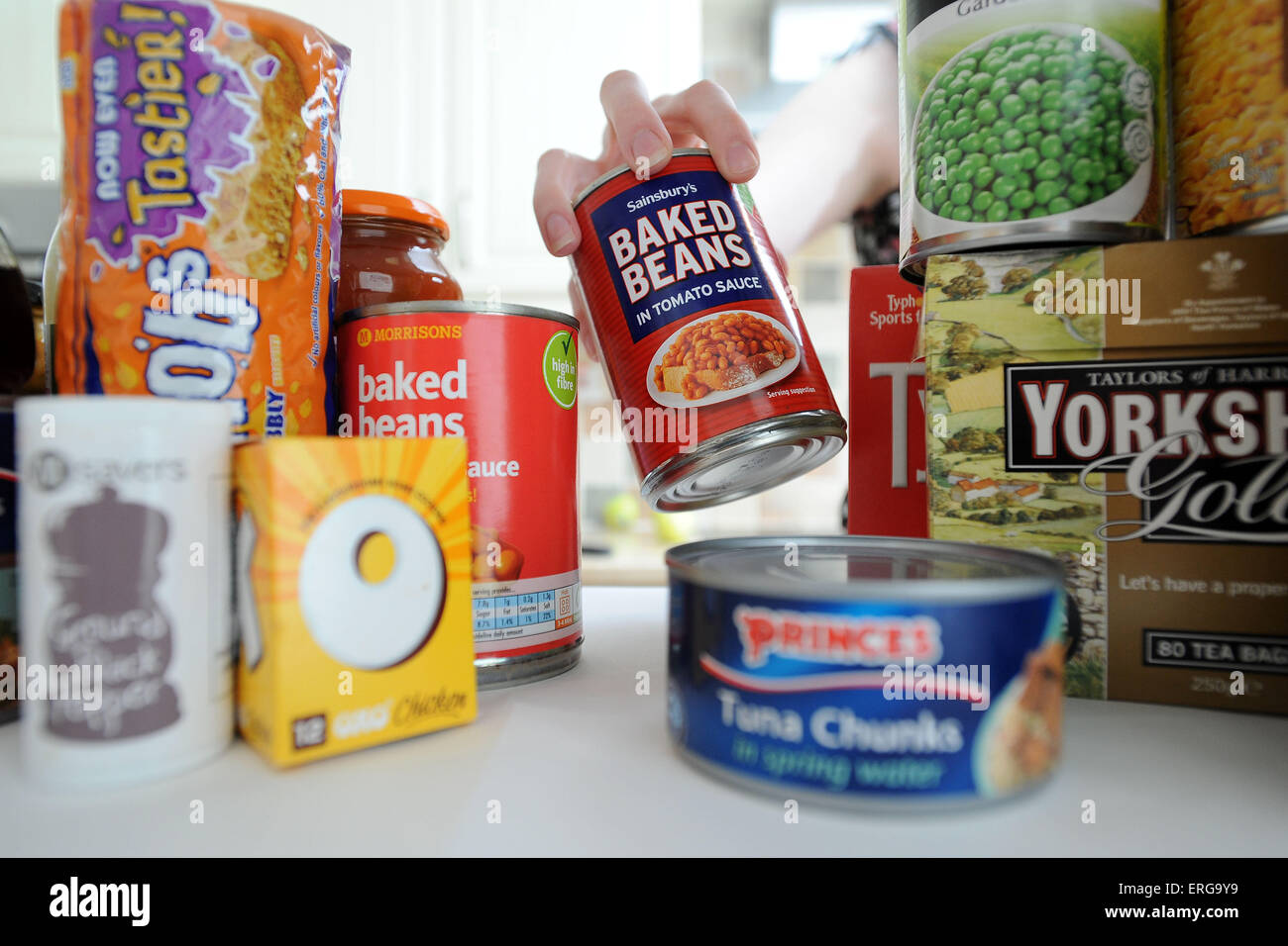 A hand grabbing a can of beans from a household cupboard full of ...