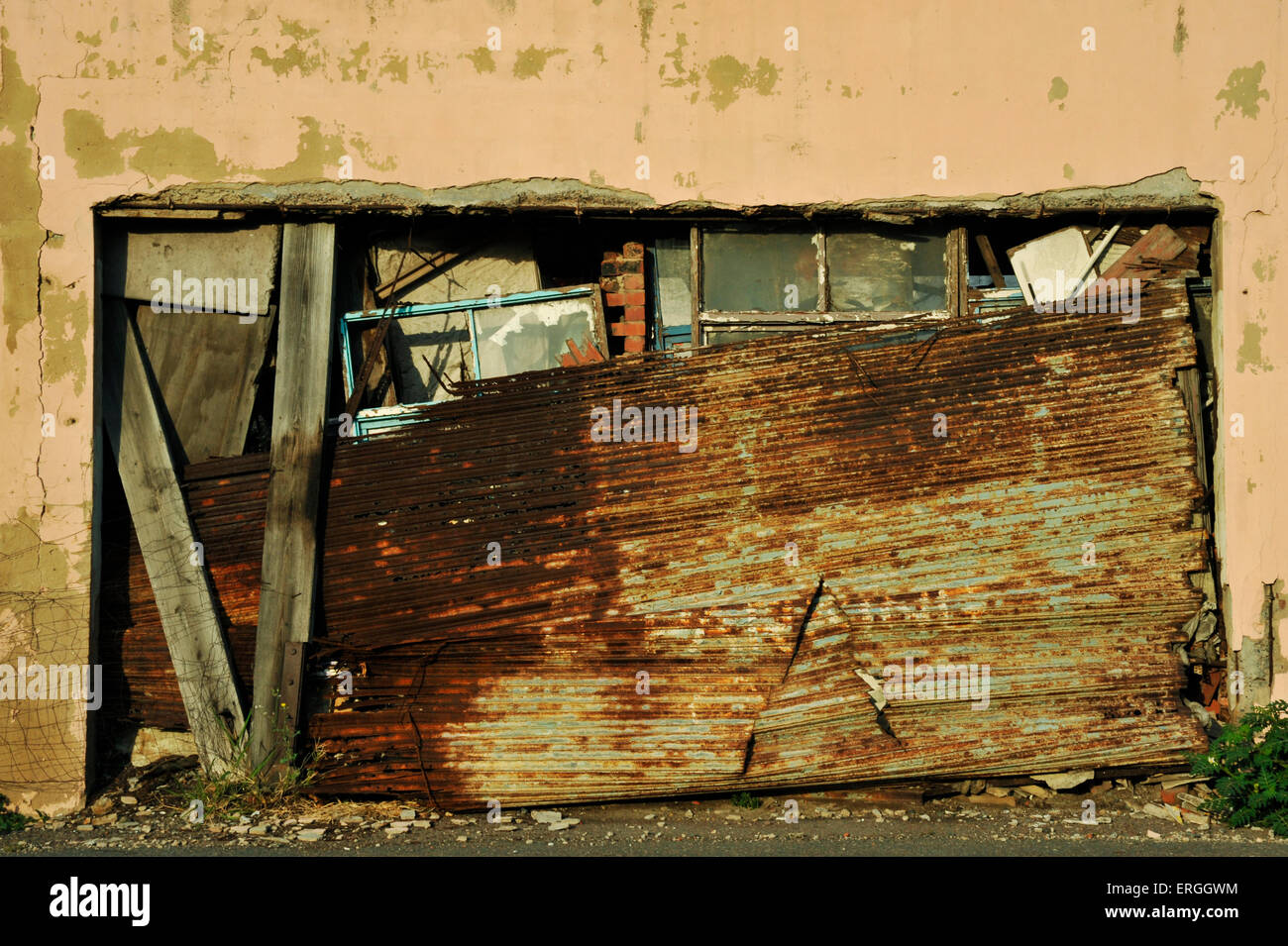 Disorderly window frames and junk supporting rusting metal garage door ...