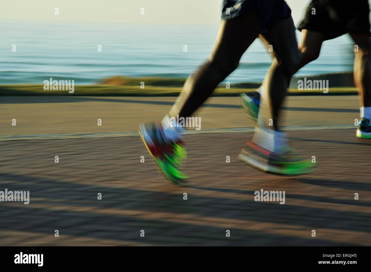 Blurred feet and legs of two athletic runners running on boardwalk next ...