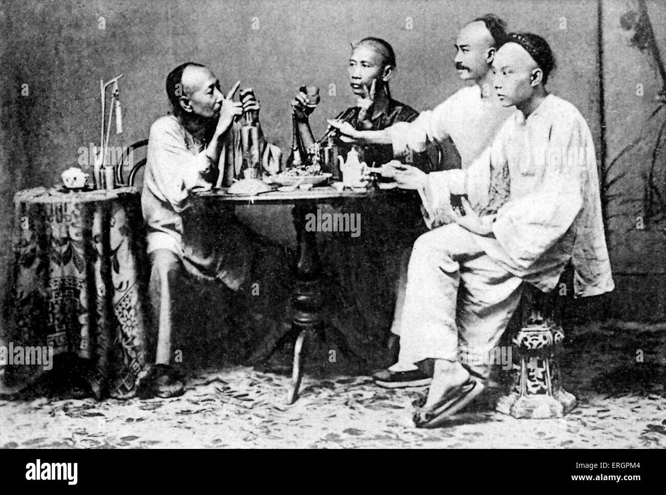 Group of men seated at table, eating with chopsticks and drinking tea ...