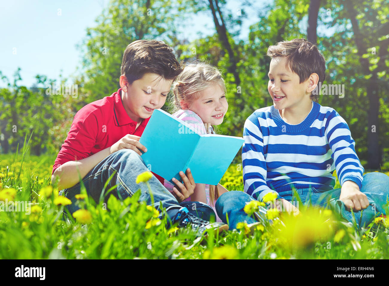 Cute children with book reading and talking on lawn Stock Photo - Alamy