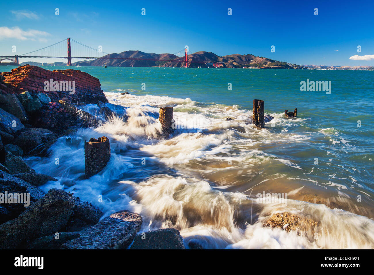 Surf splashes over dark rocks with the view of Golden Gate Bridge Stock ...