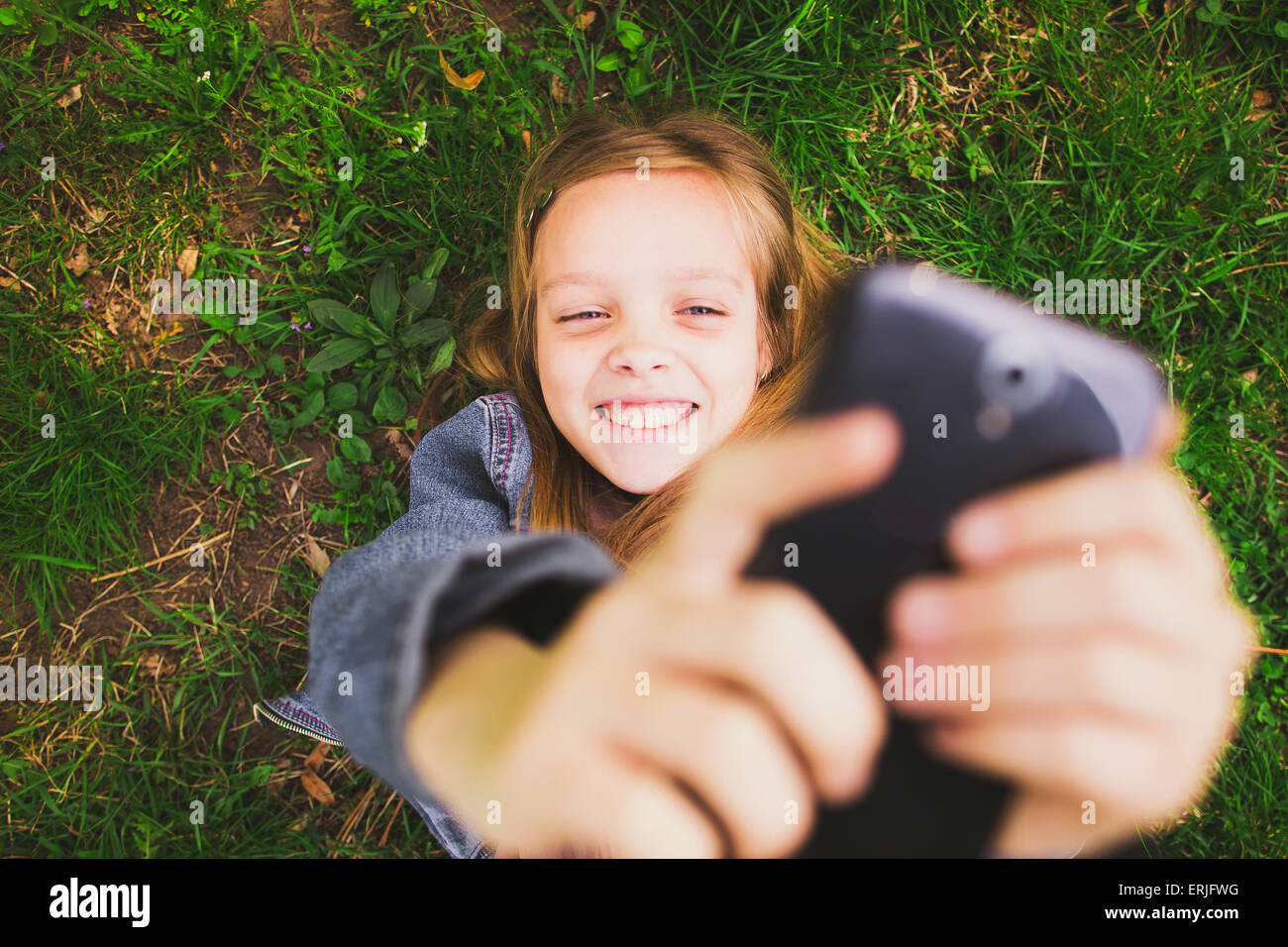 Girl laying on grass with mobile phone. Young teenager girl taking ...