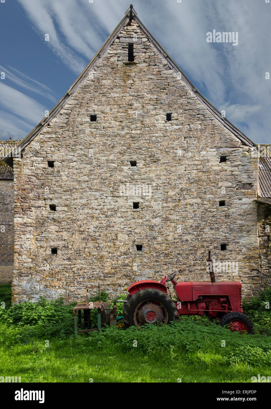 An old red tractor parked in a field of weeds in front of an old ...