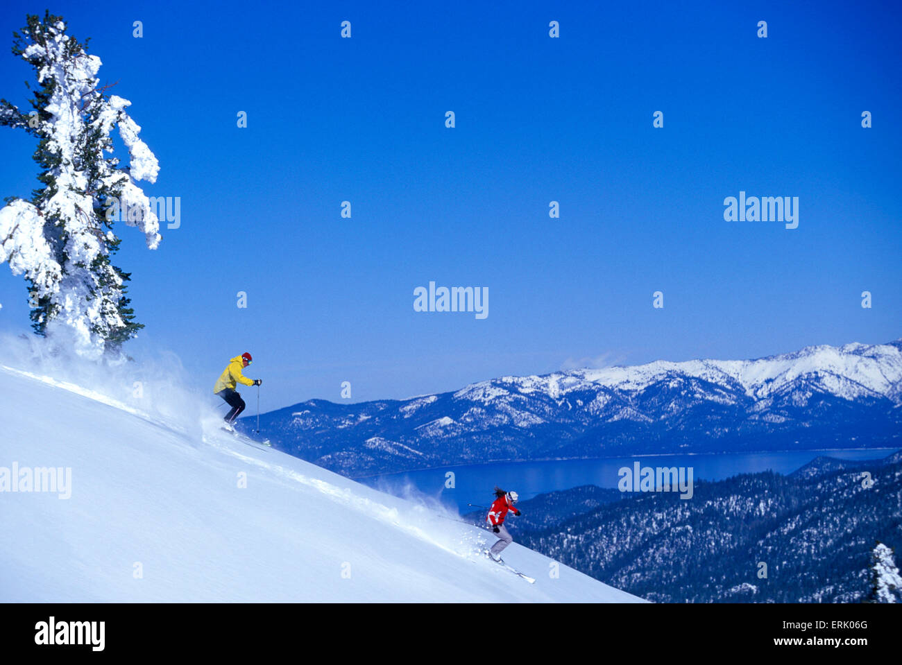 Two skiers making fresh tracks in deep powder above a blue lake Stock ...