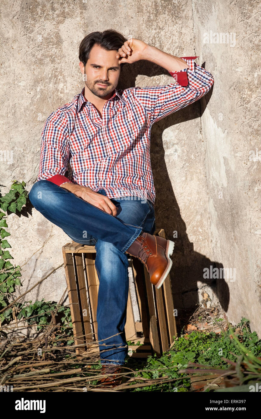 Smiling male model sitting on wooden crate with legs crossed Stock ...