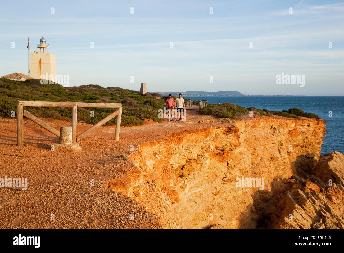 Pedestrians walk on a path on a cliff ledge with lighthouse on the ...