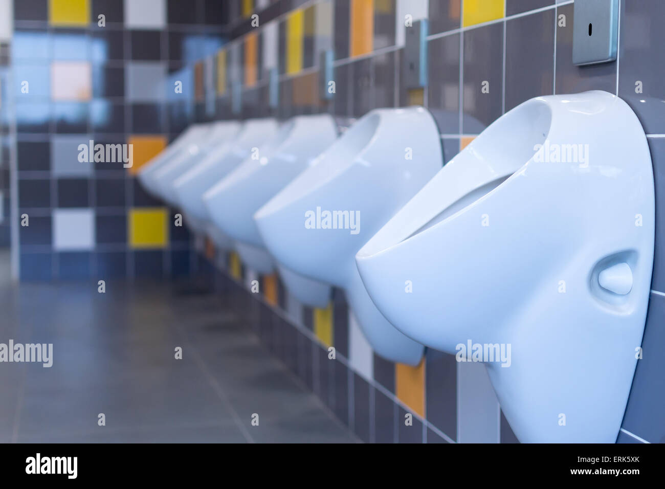 White porcelain urinals against a yellow and orange tiled wall Stock ...