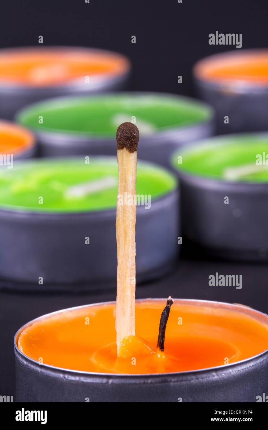 Close up detailed front view of a match, in front of candles, on black ...
