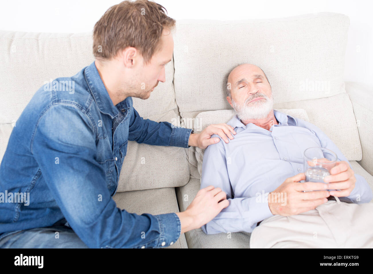 Elderly son takes care of ill father with closed eyes on the sofa Stock ...
