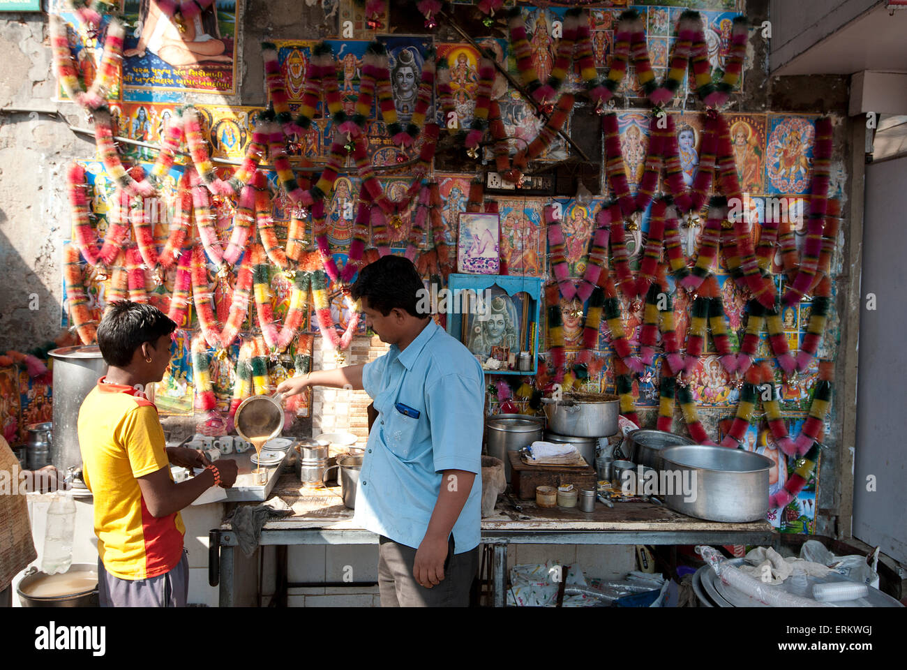 Chai wallah pouring chai (tea) at chai stall decorated with religious ...
