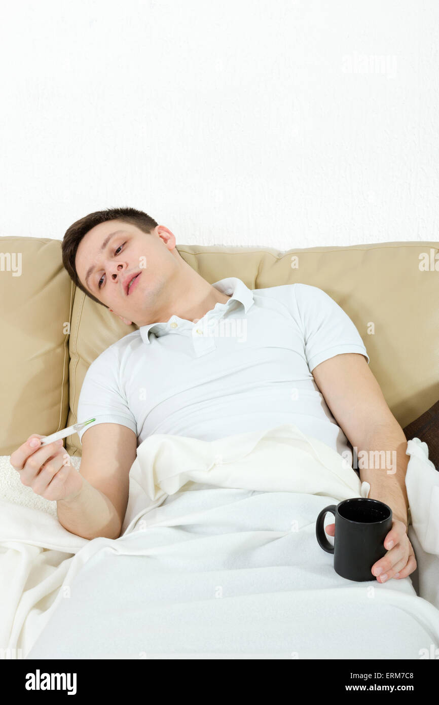 Sick man with fever laying in bed measuring temperature with ...