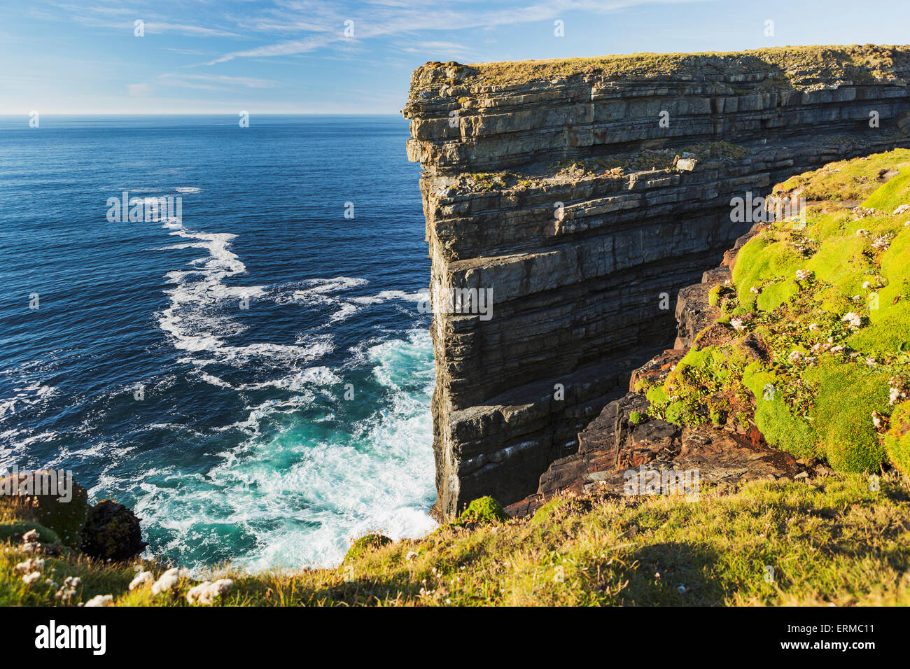 Cliff face rock formation in ocean with waves, blue sky and clouds ...
