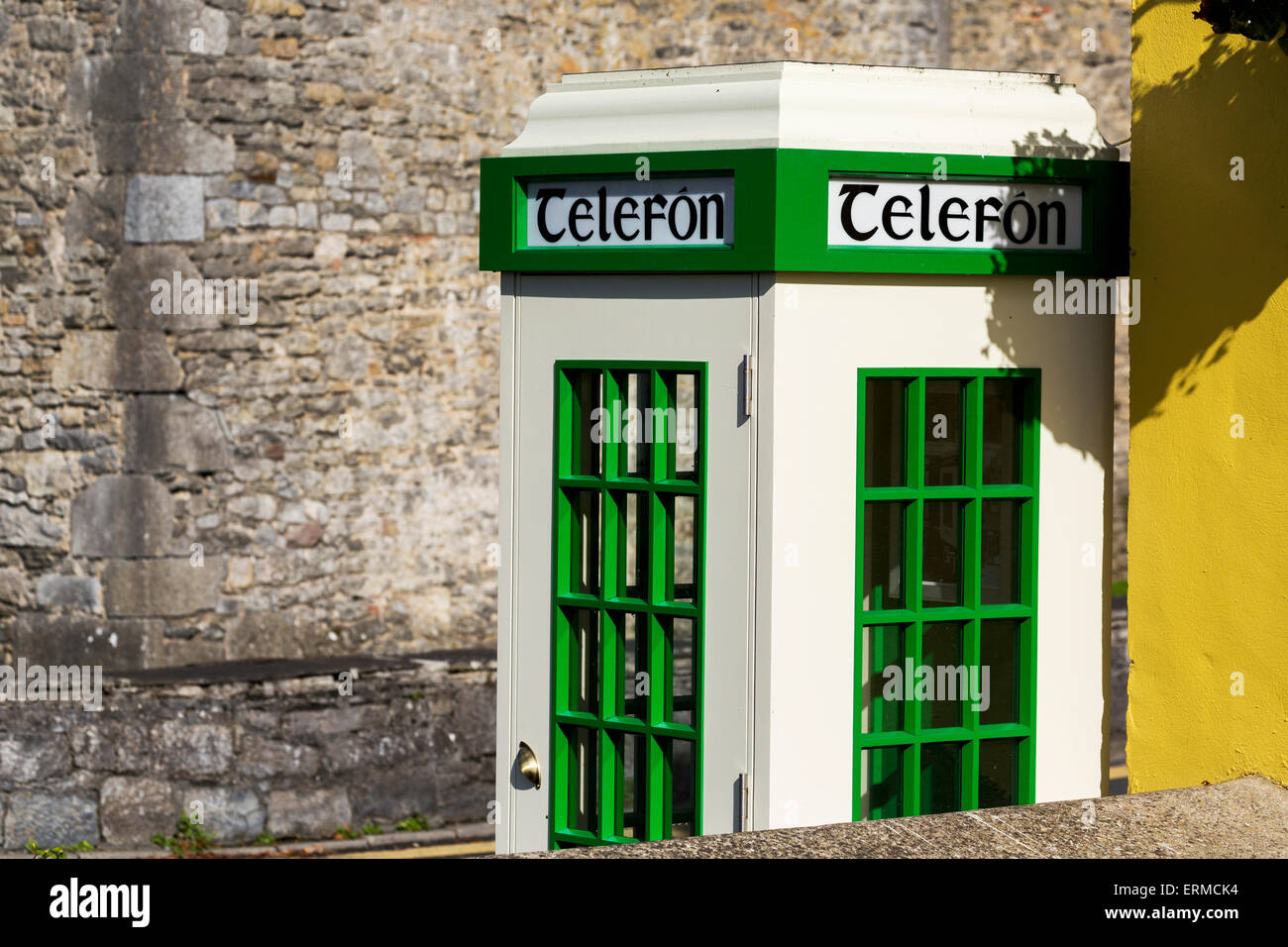 Close up of white telephone booth with green trim against a stone wall ...