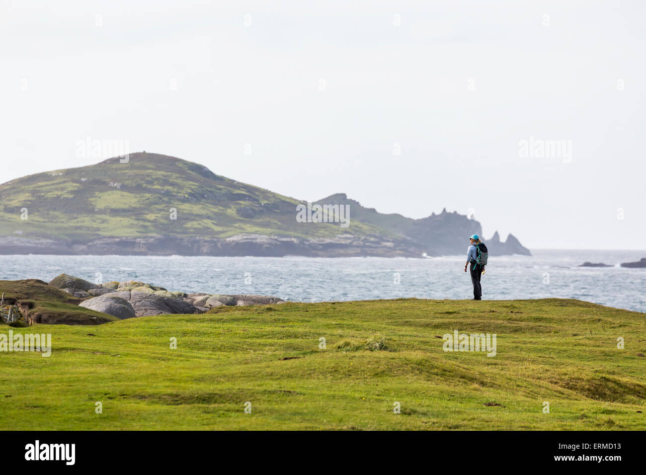 Female hiker on grassy field overlooking the ocean with large island in ...