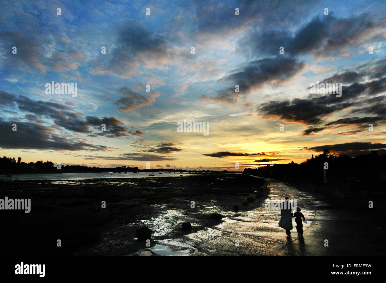 A mother and sun walk along a coastal road under a dramatic sunset ...