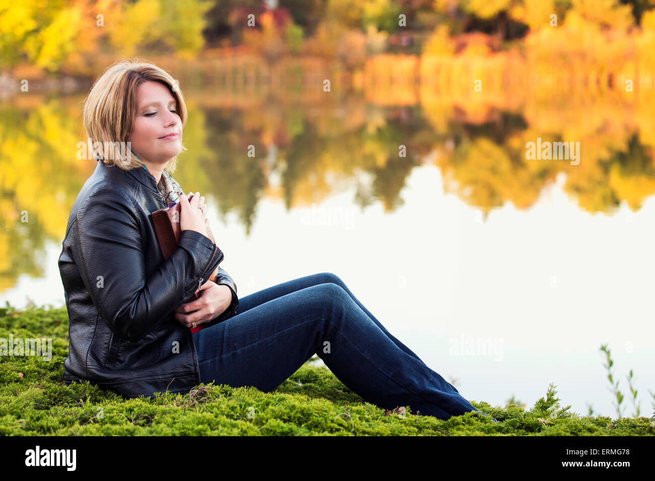 Mature Christian woman embracing her Bible in a city park beside a lake ...