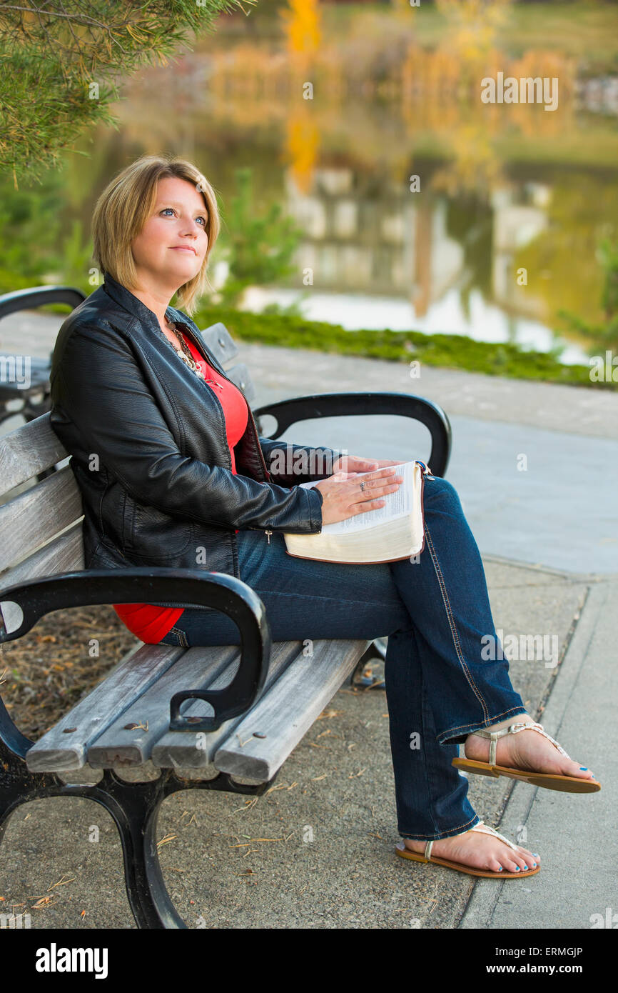 Mature Christian woman studying her Bible in a city park setting beside ...
