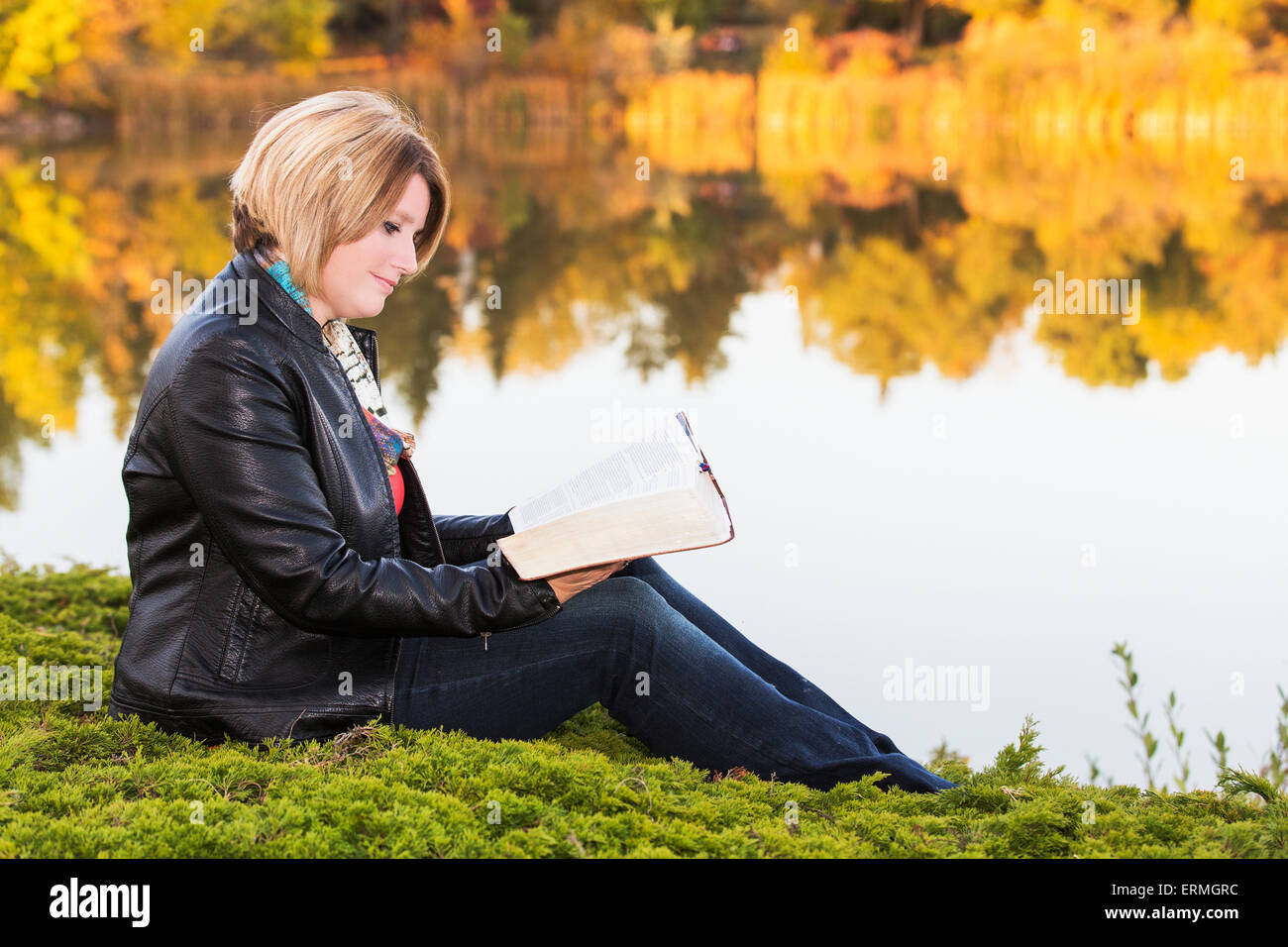 Mature Christian woman studying her Bible in a park beside a lake in ...