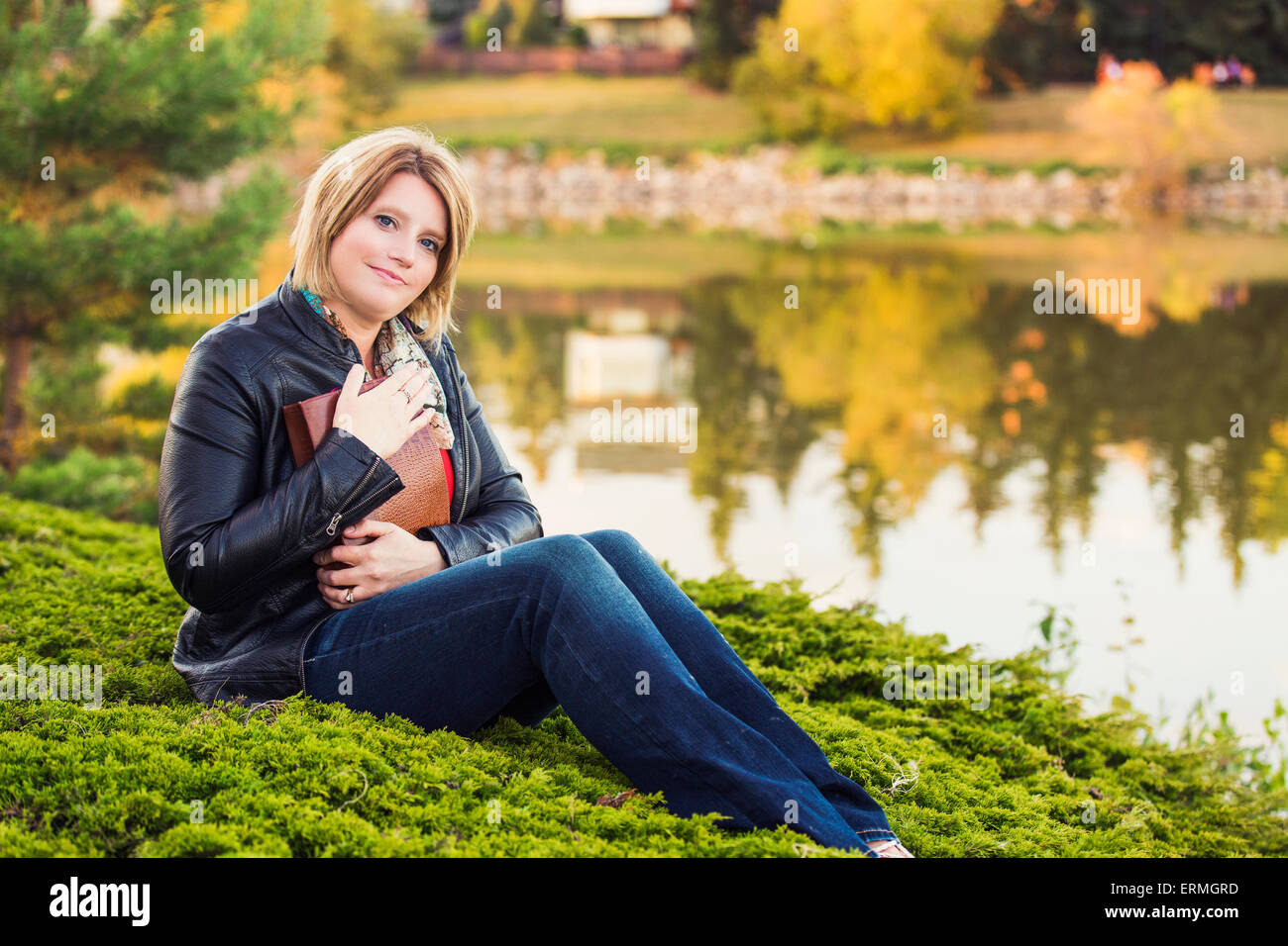 Mature Christian woman embracing her Bible in a park beside a lake in ...