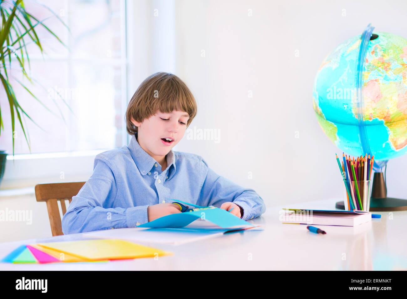 Happy smiling school boy, smart student, doing homework cutting paper ...