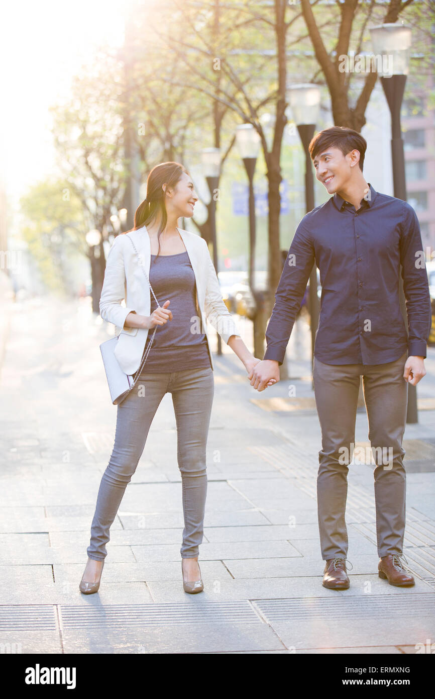 Young couple holding hands walking on sidewalk Stock Photo - Alamy