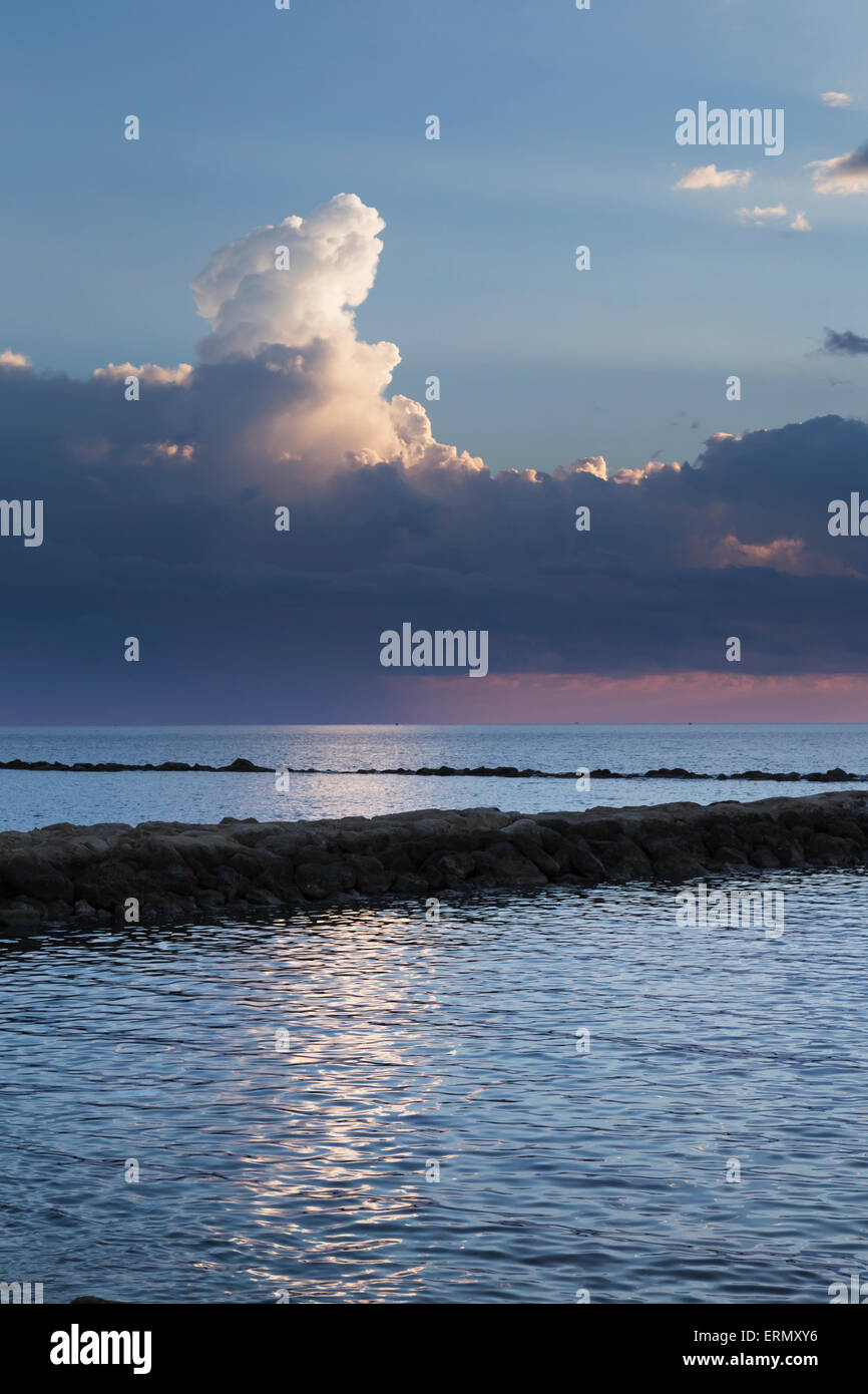 Breakwater off the coast with pink clouds on the horizon at sunrise ...