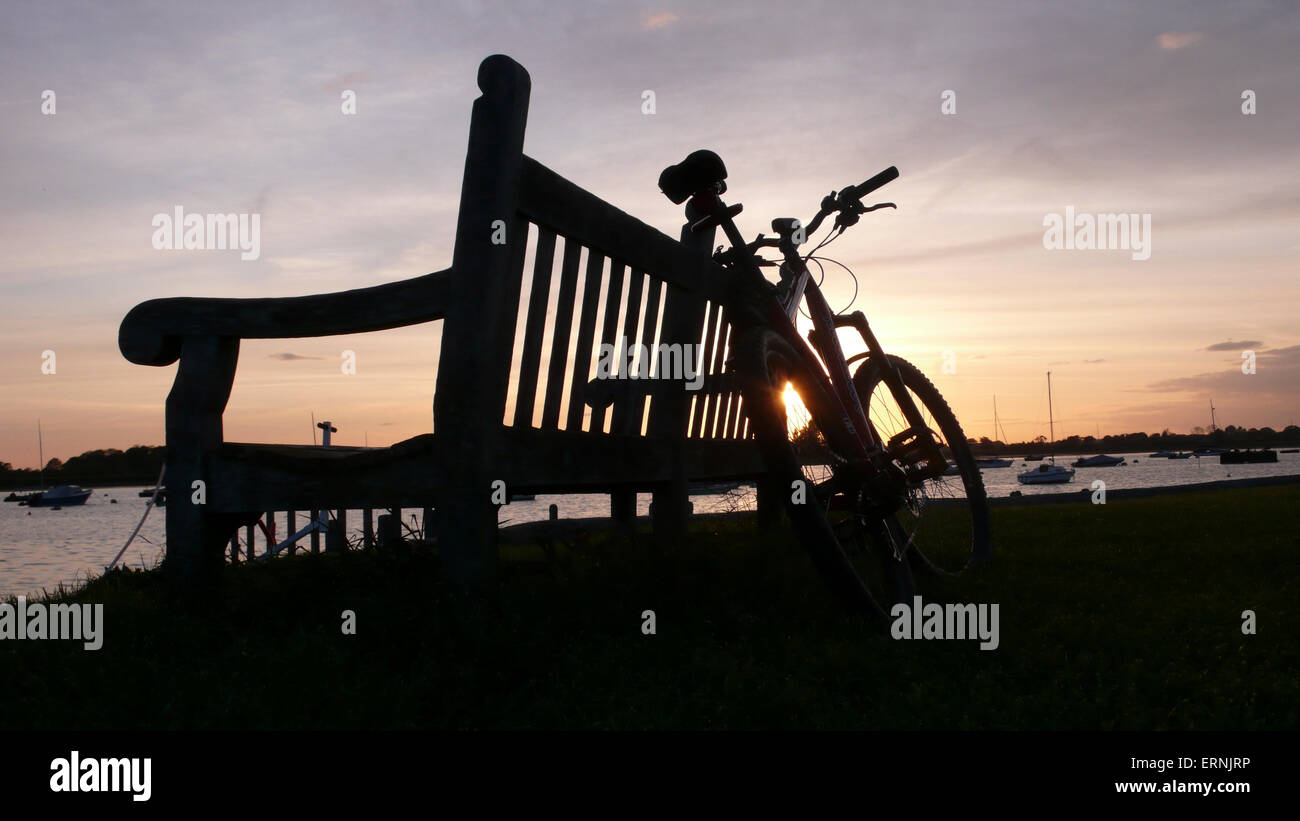 A bike leans against a bench by the seaside as the sun goes down Stock ...