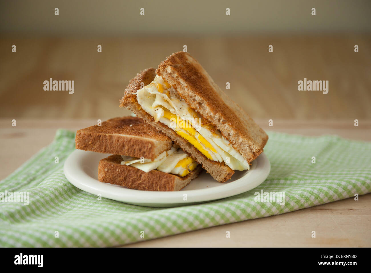 A fried egg sandwich on whole grain toast sits on a white plate atop a ...