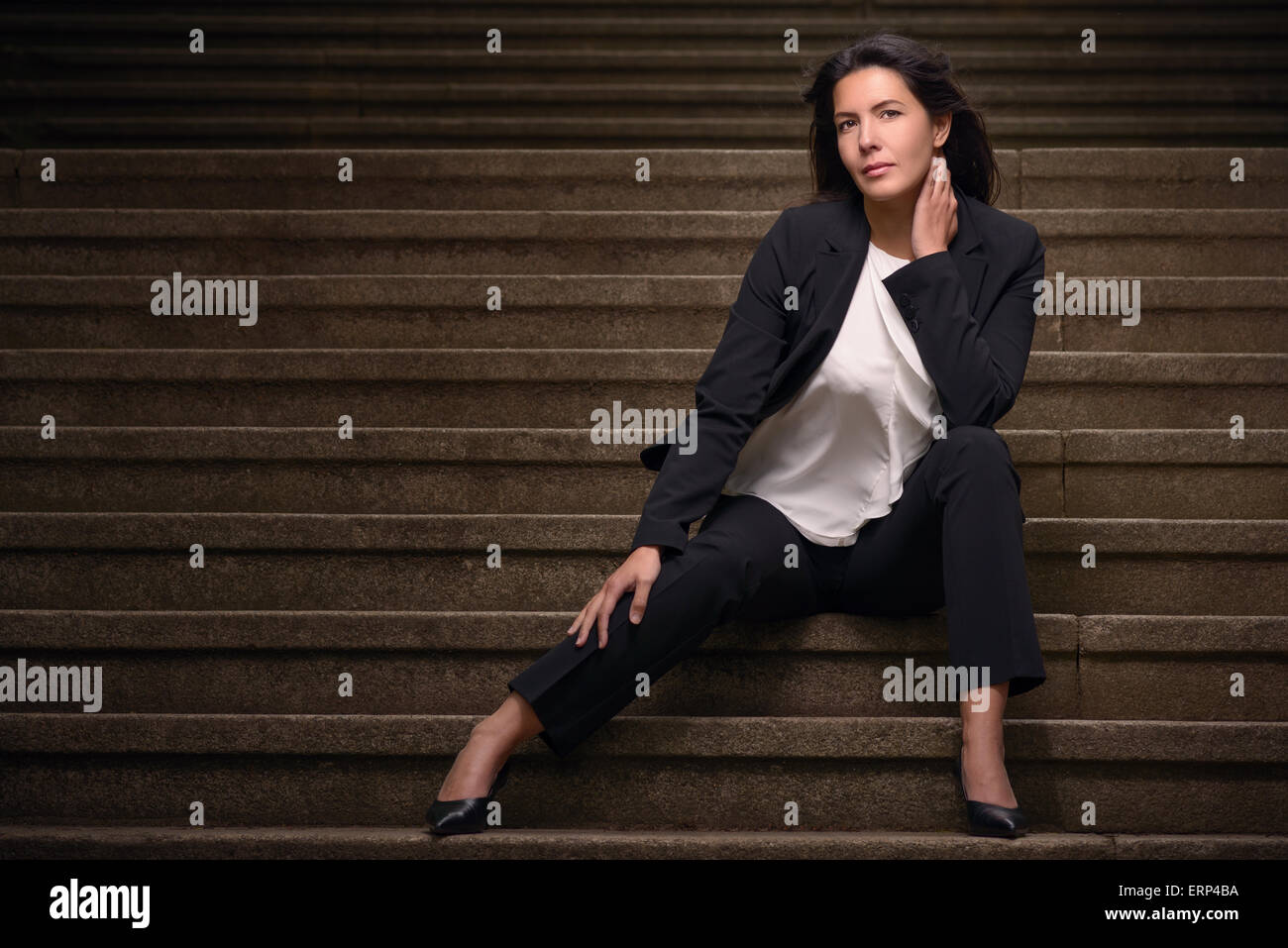 Attractive brunette woman in a slack suit sitting on urban stairs ...
