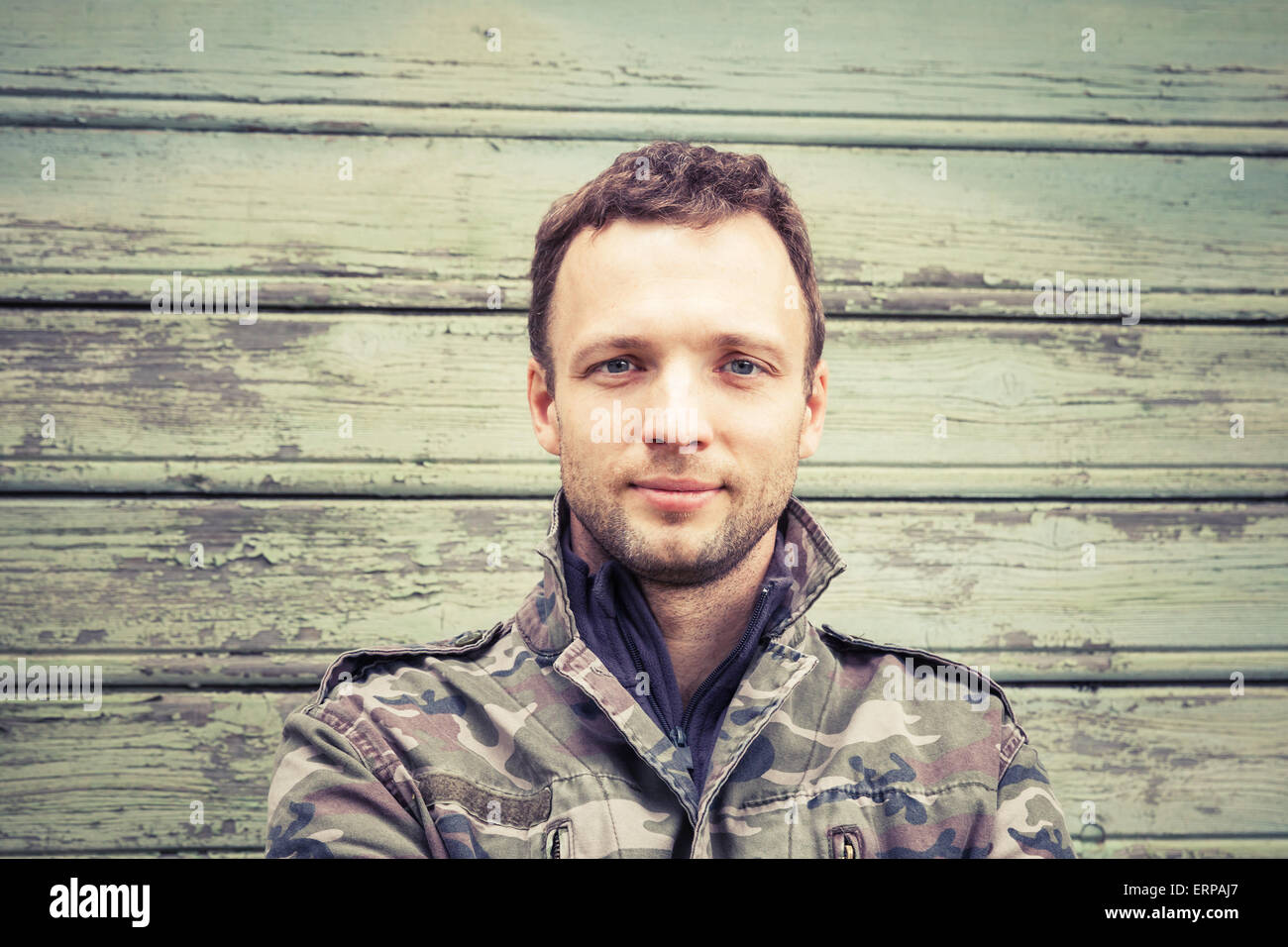 Young Caucasian man in camouflage. Outdoor portrait over green rural ...