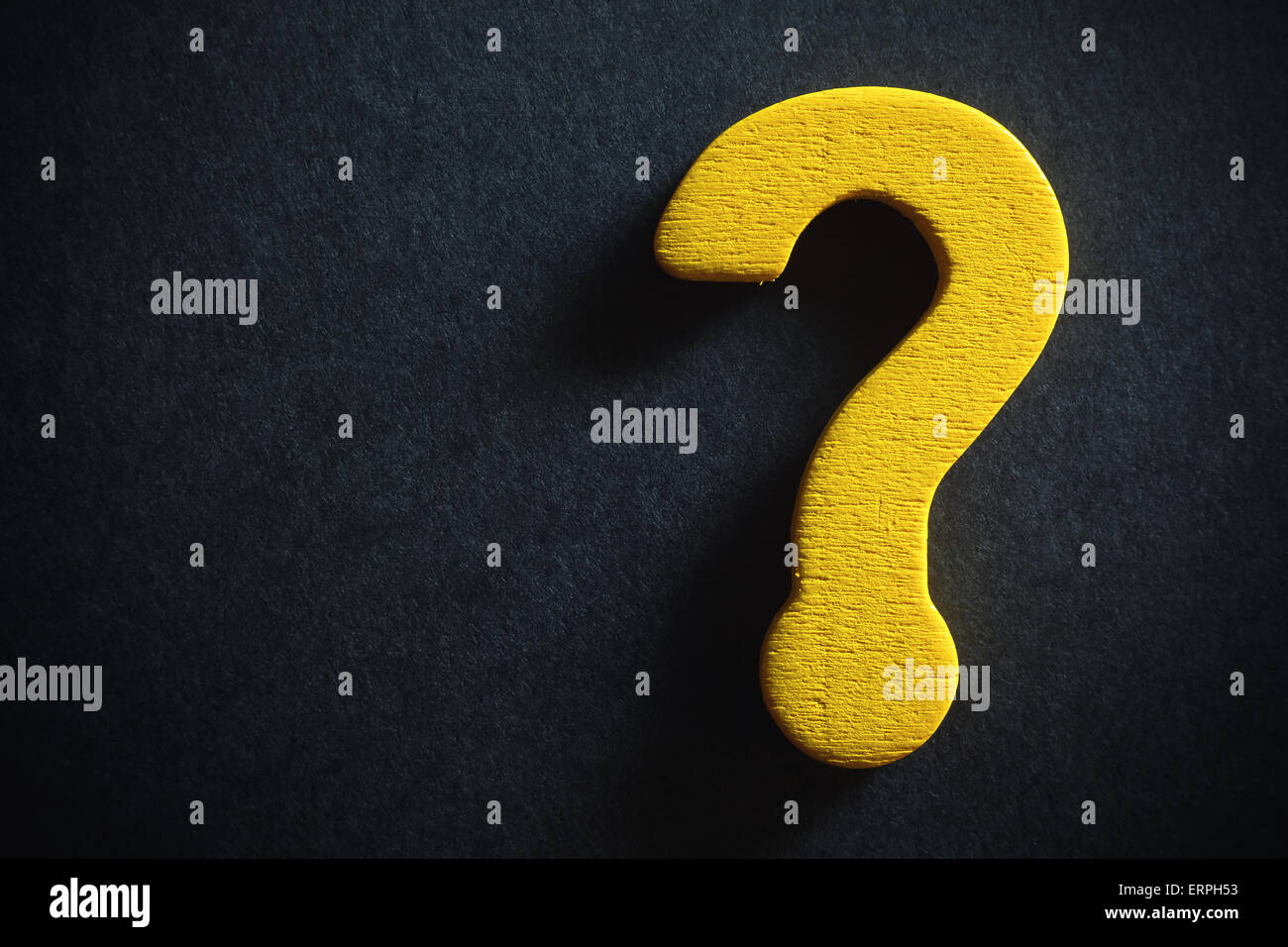 Wooden yellow question mark on black background, empty dark space on ...