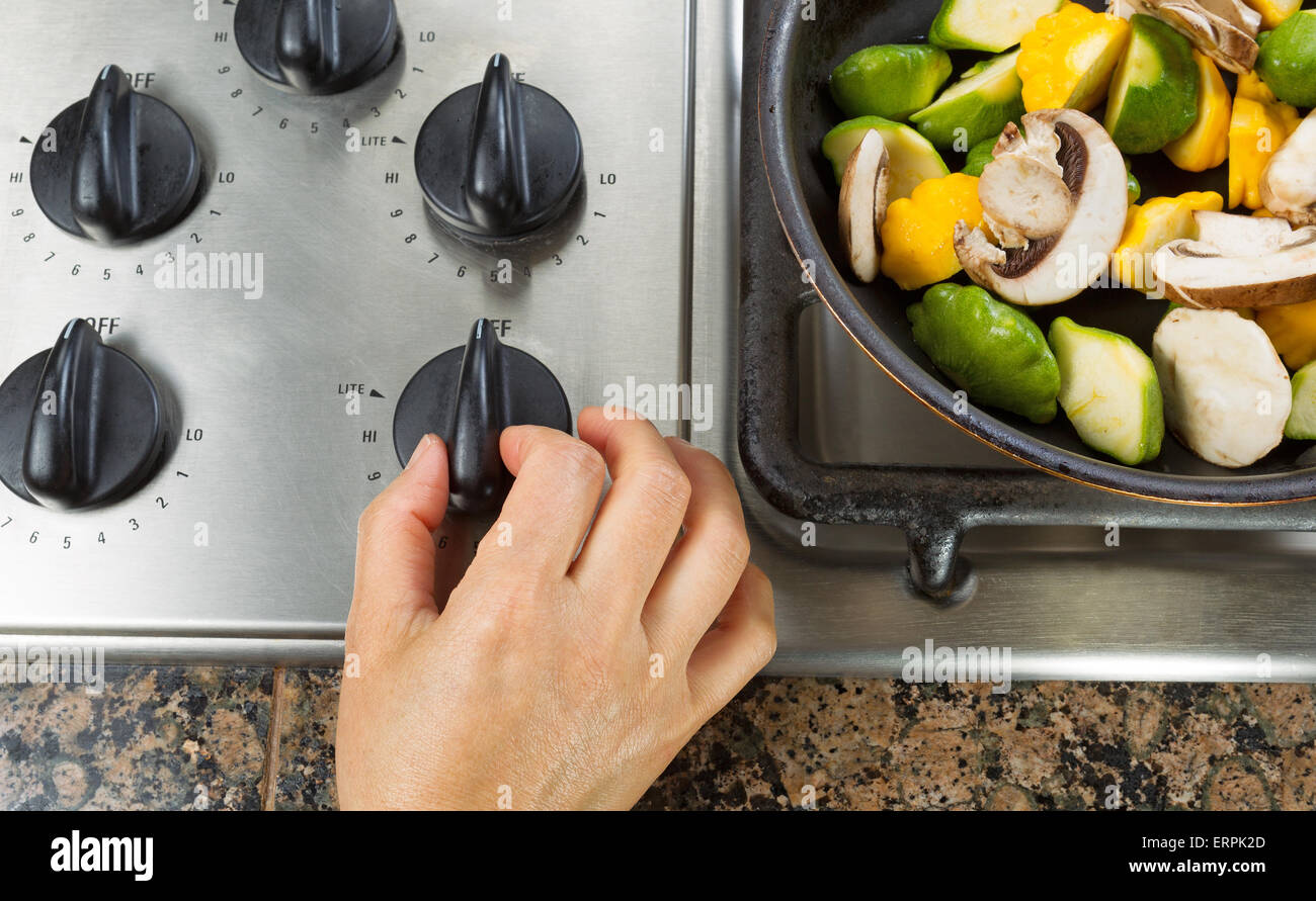 Close up of hand turning on stove with vegetables in frying pan on side ...