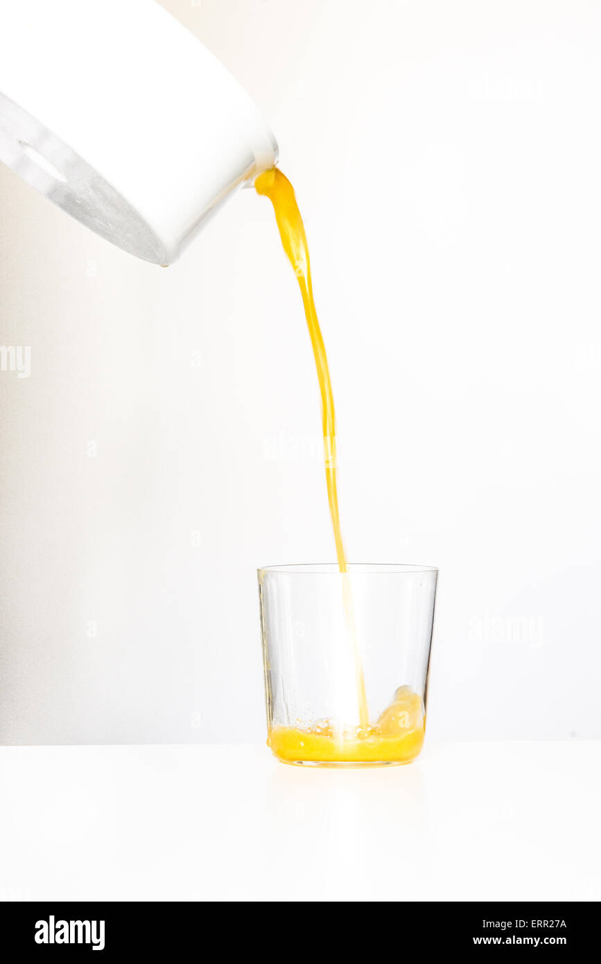 An orange juice falling into a glass on a white isolated background ...