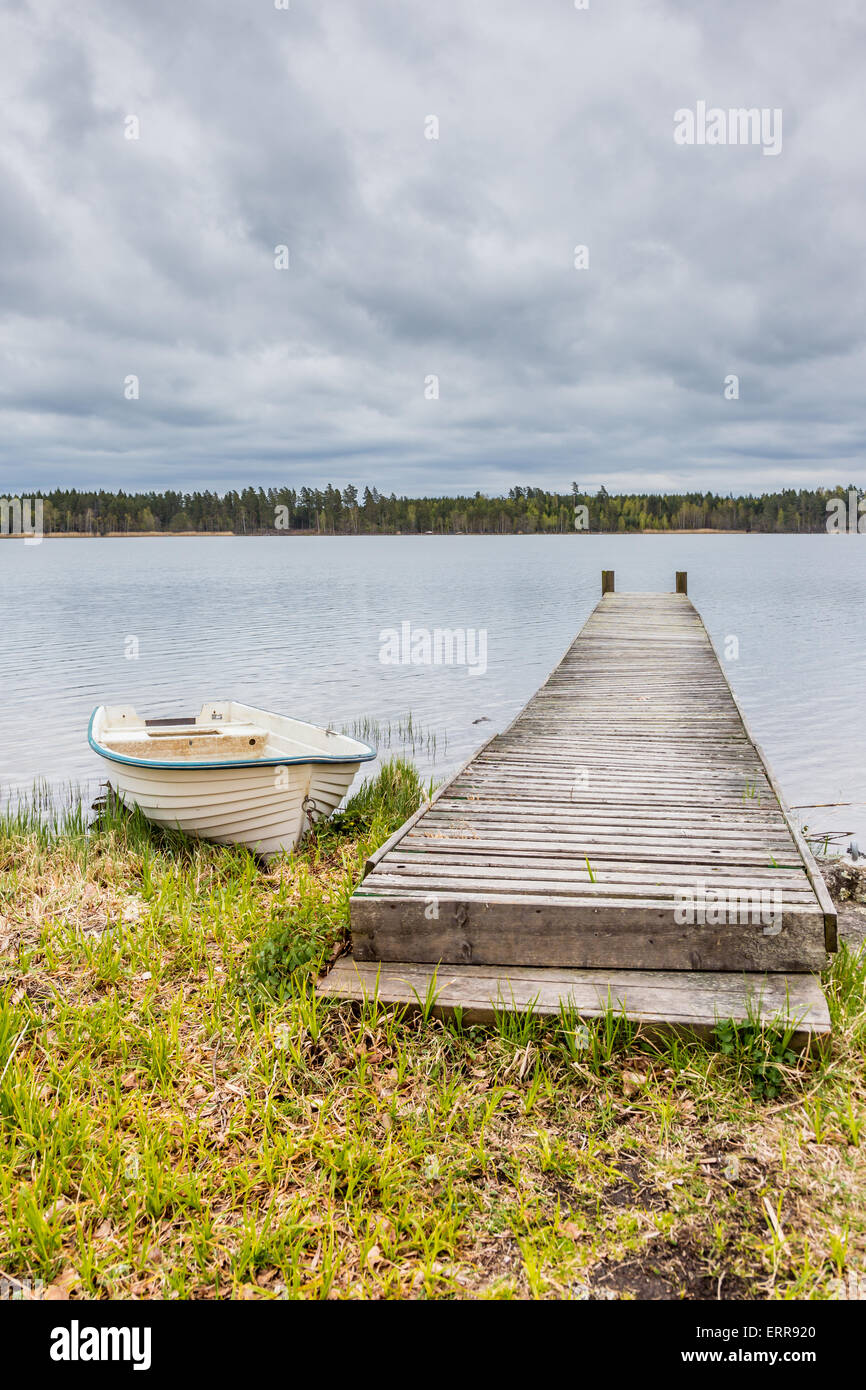 White Rowing boat Next to a Wodden Pier with a Cloudy Sky as Background ...