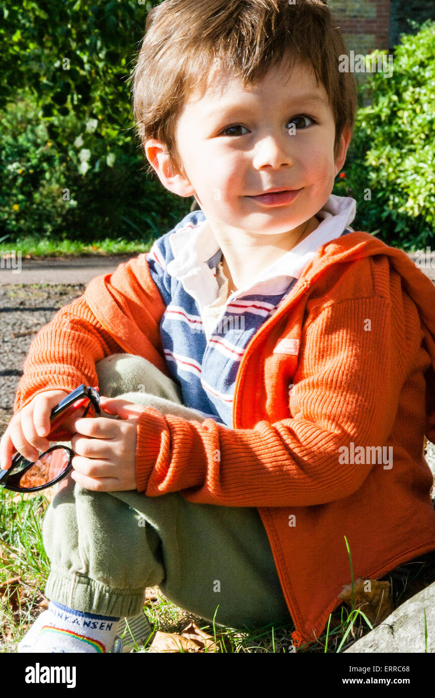 Caucasian child, boy, 3-4 year old, sitting outdoors with back against ...