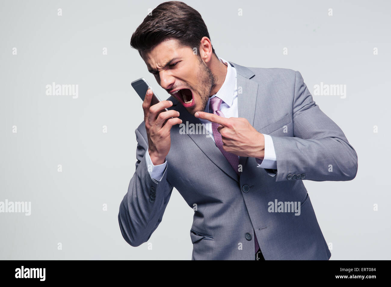 Angry businessman shouting on the phone over gray background Stock ...