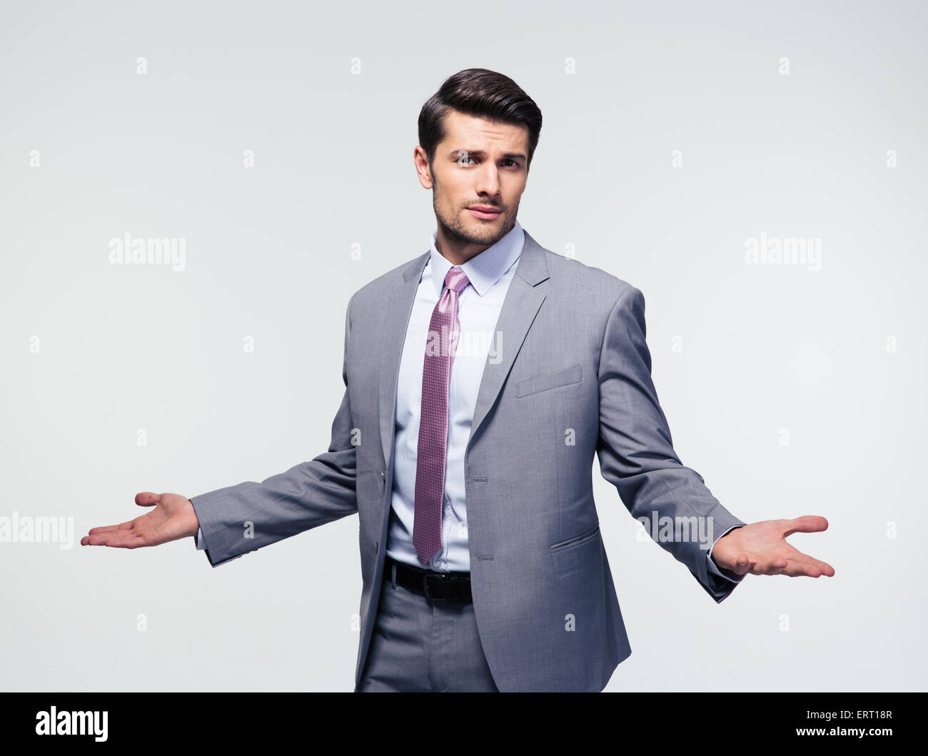 Businessman shrugging shoulders over gray background. Looking at camera ...