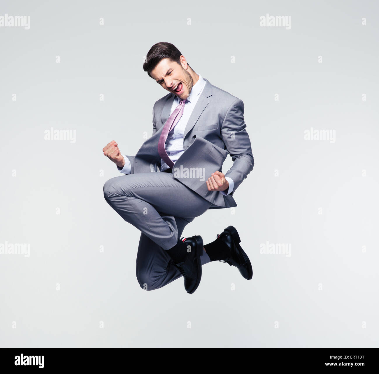 Funny cheerful businessman jumping in air over gray background Stock ...