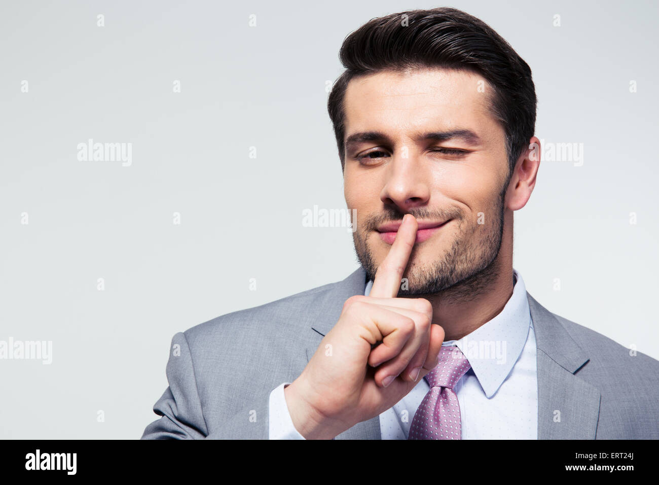 Businessman pointing finger over lips, asking for silence over gray ...