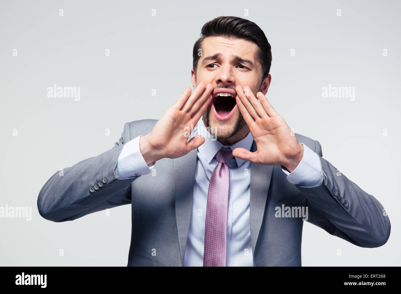 Handsome businessman shouting over gray background and looking away ...